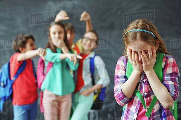 Unhappy schoolgirl hiding her face on background of teasing classmates ... Unhappy schoolgirl hiding her face on background of teasing classmates ...
