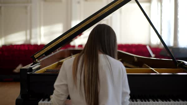 Close-up view from back of unrecognizable female pianist with long black hair repetition playing ...