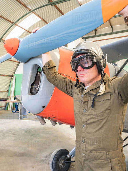 Confident pilot beside retro plane in hangar - Royalty-free Stock Photo | Dissolve