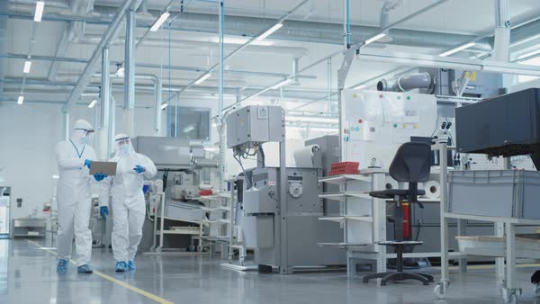 Two Scientists in Sterile Coveralls Walking in a Heavy Industry Factory with Laptop Computer ...