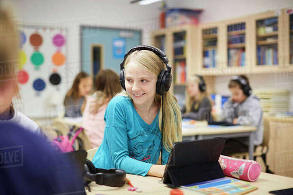 Smiling girl wearing headphones while using digital table in classroom ...