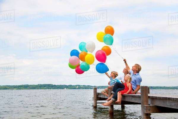 Family holding balloons on wooden pier - Royalty-free Stock Photo | Dissolve