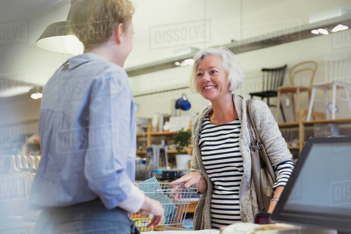 Female shopper and cashier talking at checkout counter in shop ...