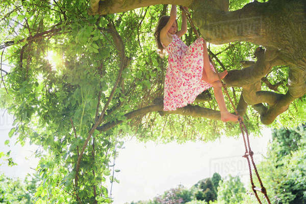 Girl in sun dress climbing tree - Royalty-free Stock Photo | Dissolve
