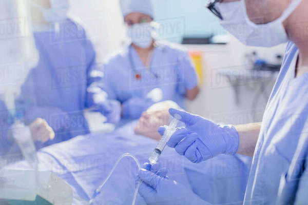 Anesthesiologist with syringe injecting anesthesia into IV drip in ...