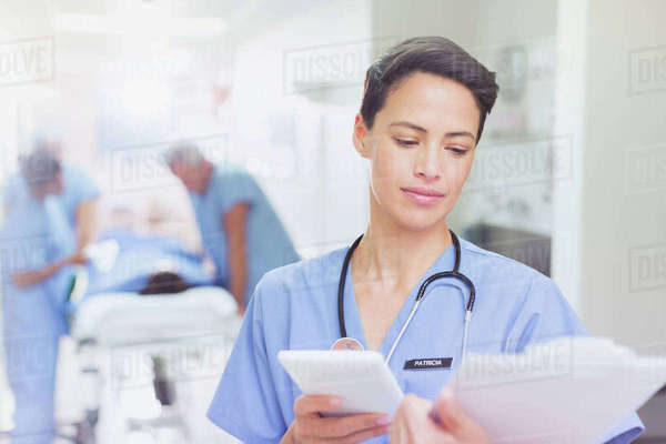 Female surgeon with digital tablet reviewing clipboard paperwork in ...