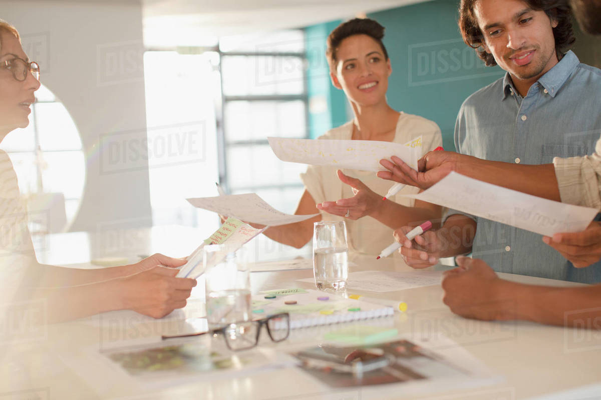 Creative business people brainstorming, passing paperwork in conference ...