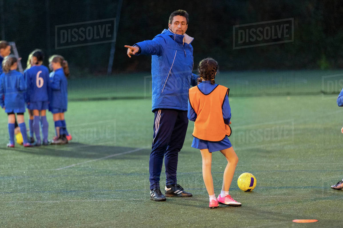 Soccer coach guiding girl soccer players practicing on field at night ...