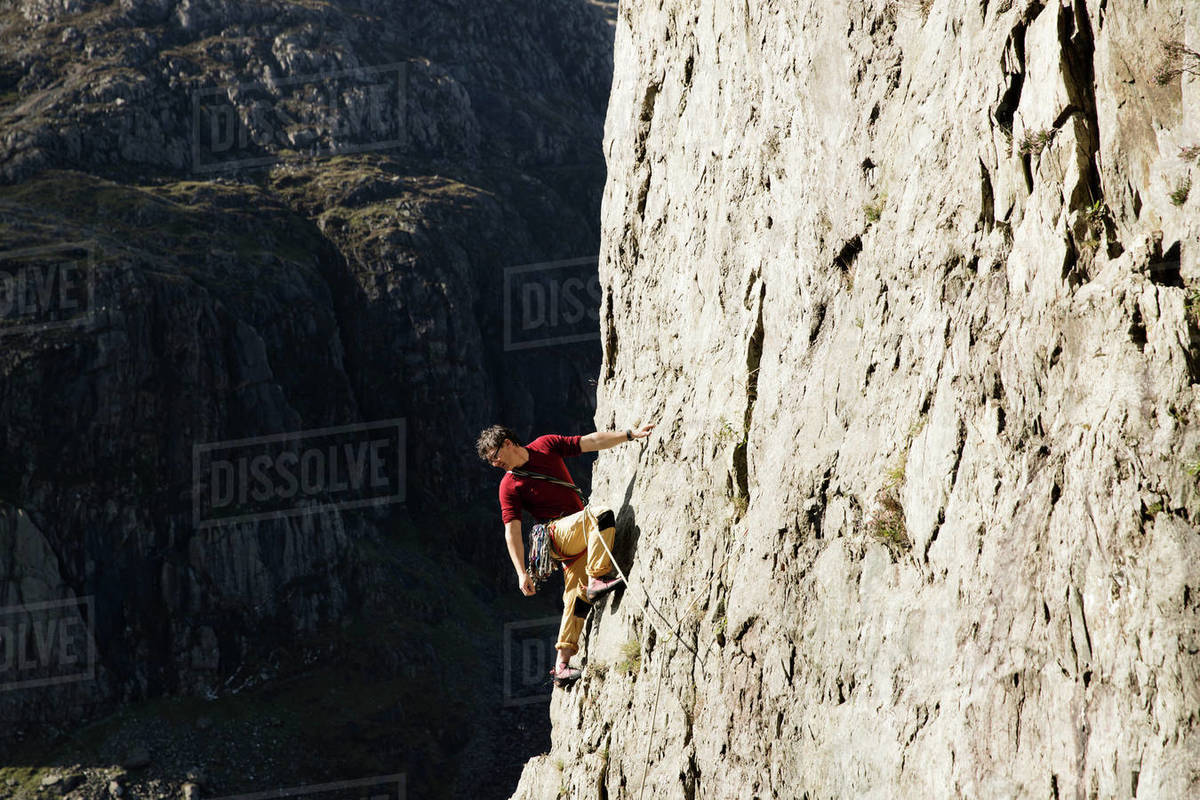 Male rock climber scaling large rock face, looking down over shoulder ...