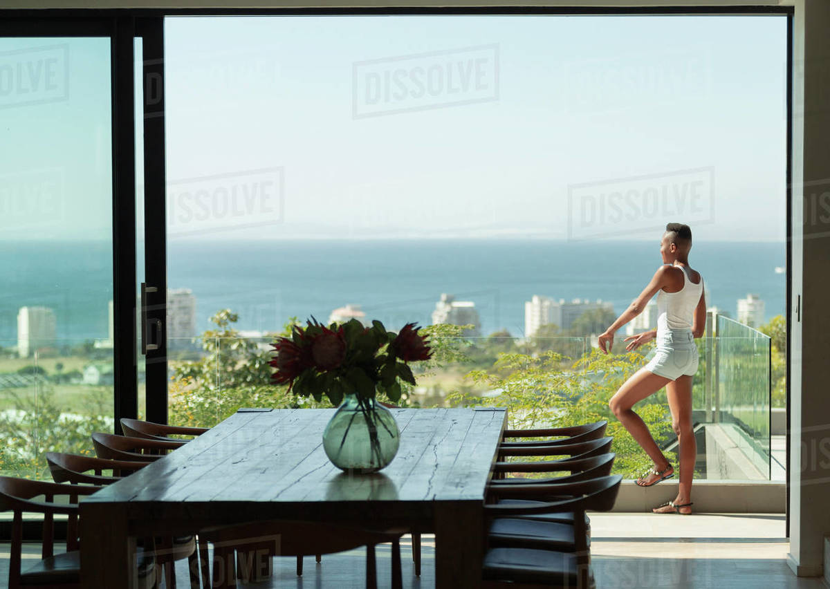 Young woman standing on modern balcony with sunny ocean view - Royalty ...