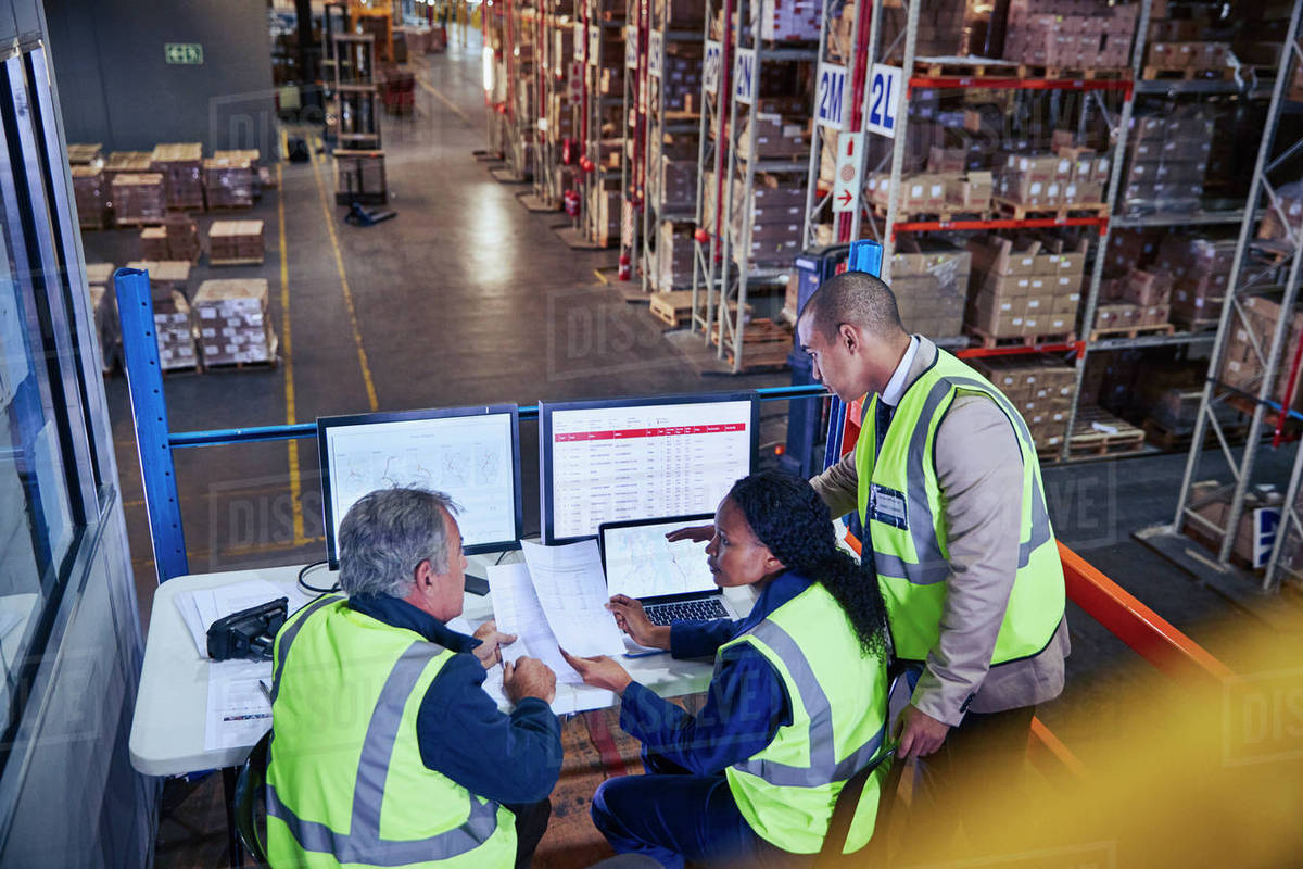 Managers at laptop and computers discussing paperwork in distribution ...