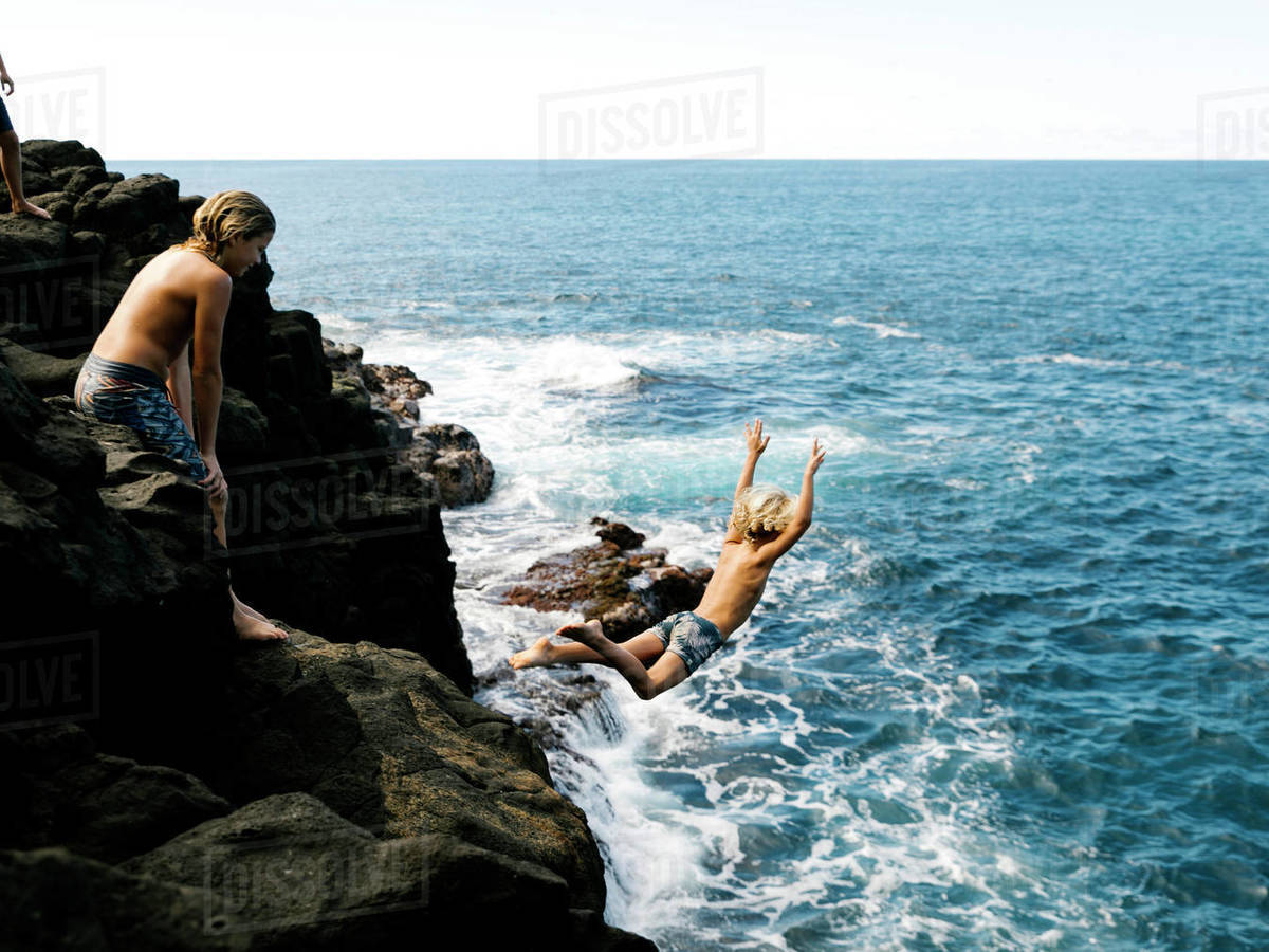 Boy jumping off cliff by sea - Stock Photo - Dissolve