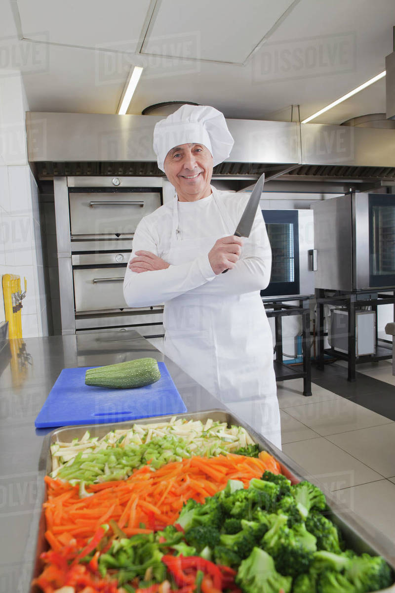 Smiling chef holding kitchen knife by raw vegetables - Royalty-free ...
