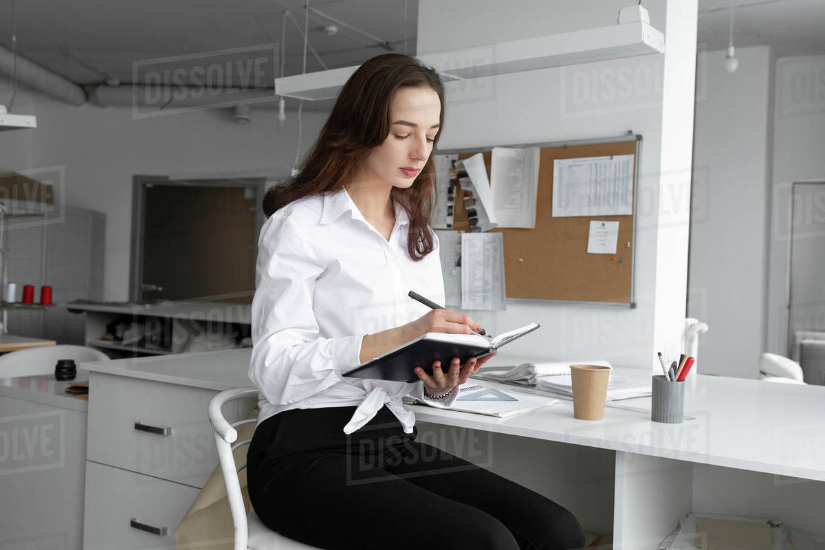 Fashion designer writing in notebook - Royalty-free Stock Photo | Dissolve