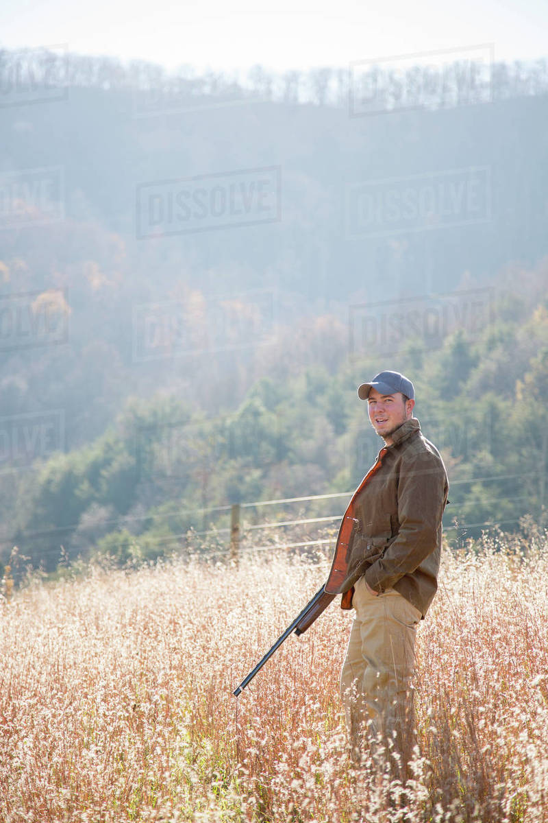 Young man holding rifle in field - Royalty-free Stock Photo | Dissolve