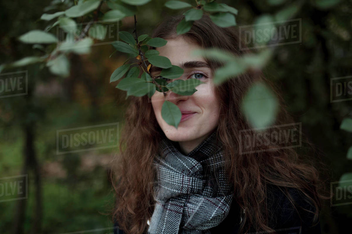 Young woman smiling behind tree branch - Stock Photo - Dissolve