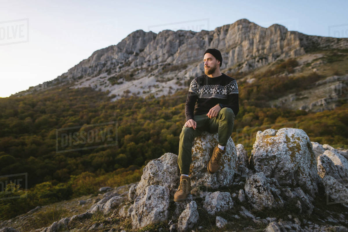 Man sitting on rock by mountain - Royalty-free Stock Photo | Dissolve