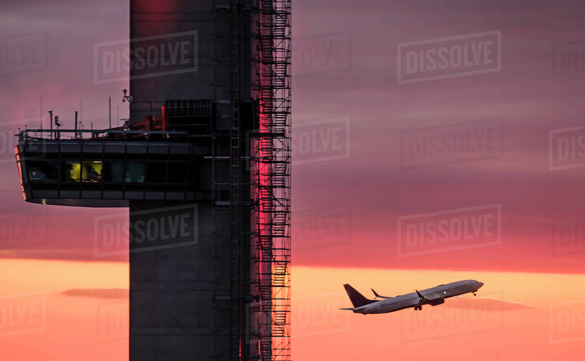Airplane flying past control tower at sunset - Royalty-free Stock Photo ...