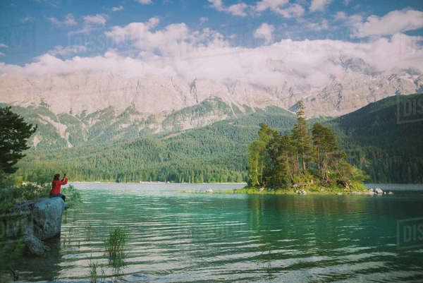 Germany, Bavaria, Eibsee, Young woman sitting on rock by Eibsee Lake in ...
