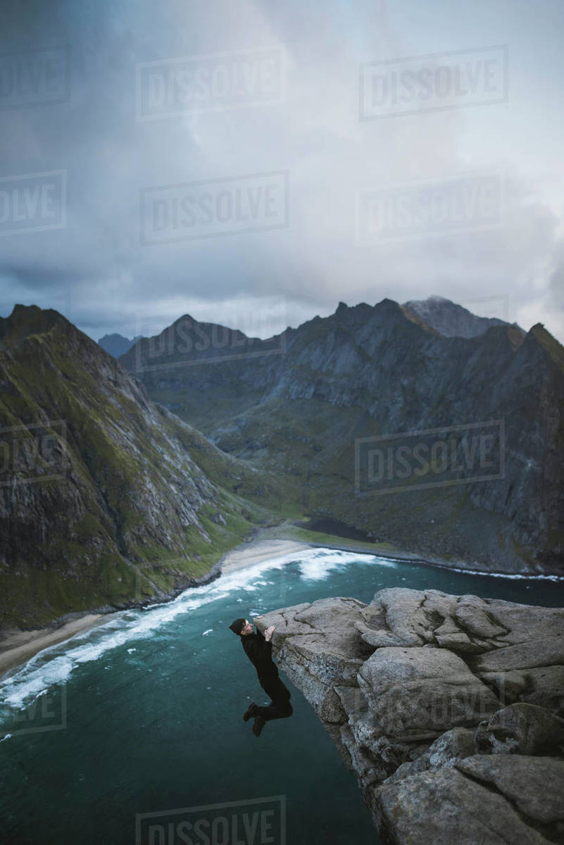 Man hanging on cliff at Ryten mountain in Lofoten Islands, Norway - Stock Photo - Dissolve
