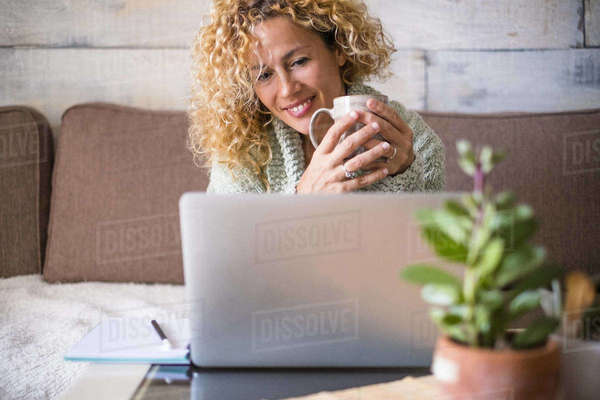 Smiling woman holding drink at laptop - Royalty-free Stock Photo | Dissolve