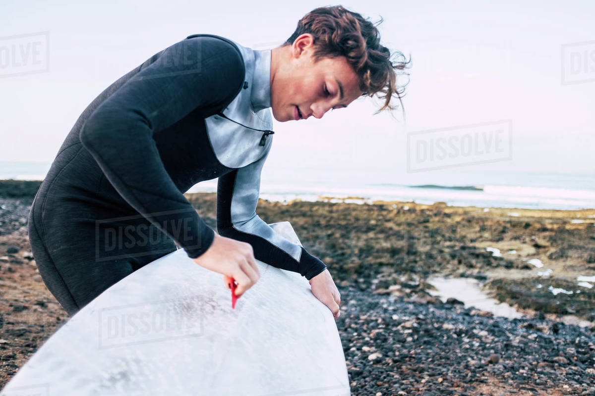 Teenage boy waxing surfboard at beach - Royalty-free Stock Photo | Dissolve