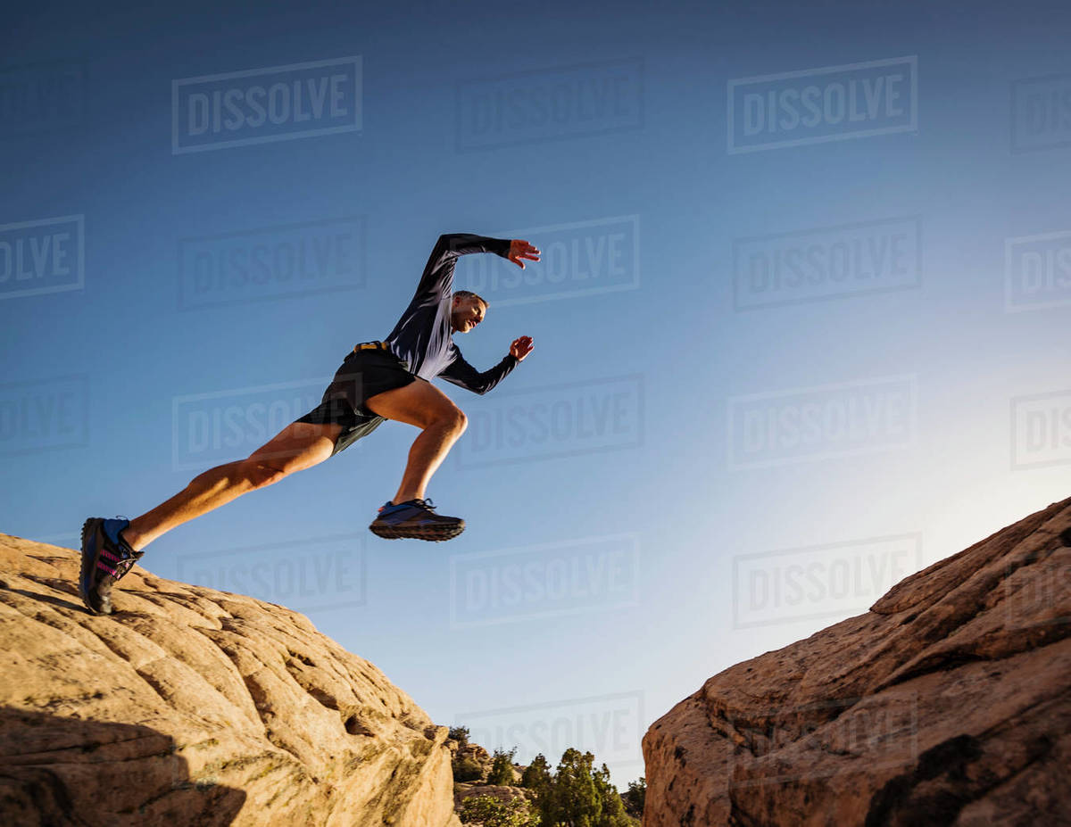 USA, Utah, St. George, Man jumping over rocks while running in eroded ...