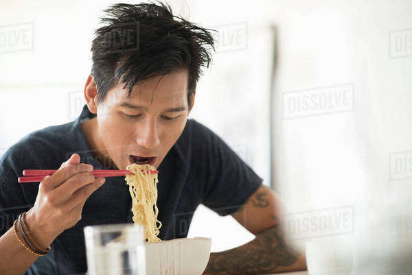 Man eating noodles with chopsticks - Stock Photo - Dissolve