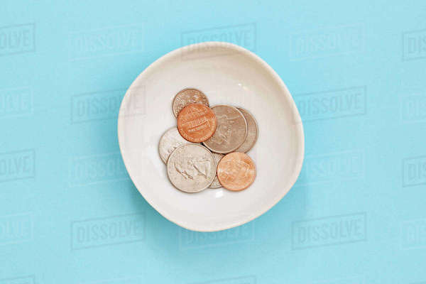 Coins in bowl on blue background - Stock Photo - Dissolve