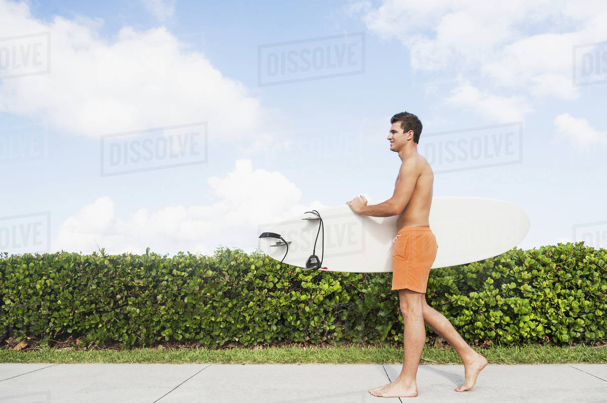 Young man carrying surfboard - Royalty-free Stock Photo | Dissolve