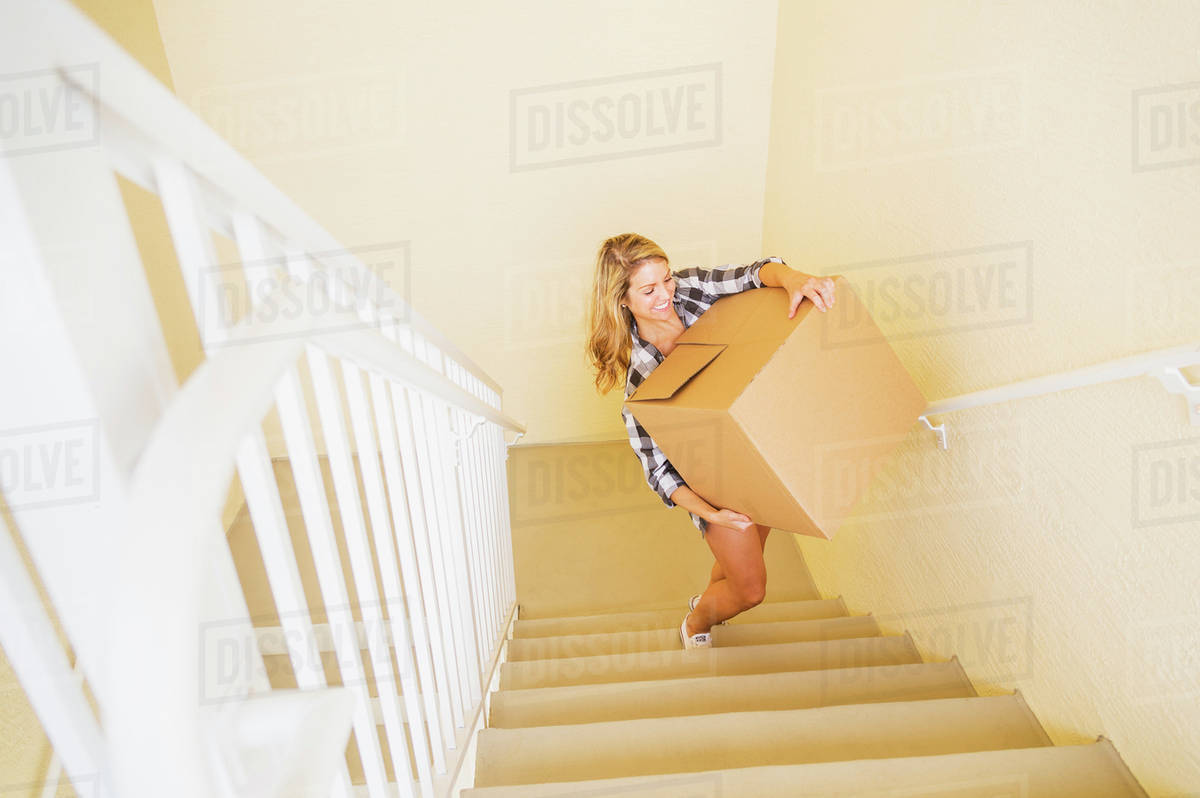 Young woman carrying box in her new house - Stock Photo - Dissolve