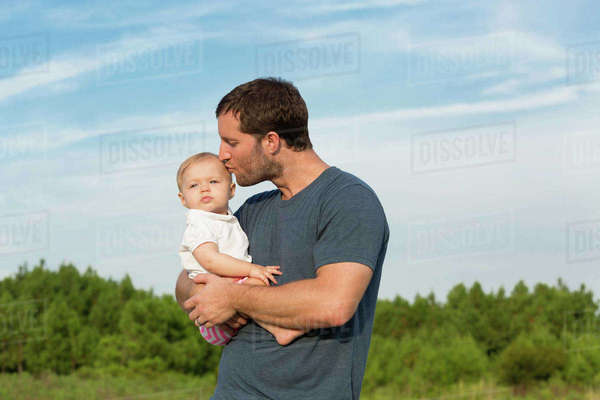 Mid adult man kissing baby daughter on cheek in rural outdoor - Royalty ...