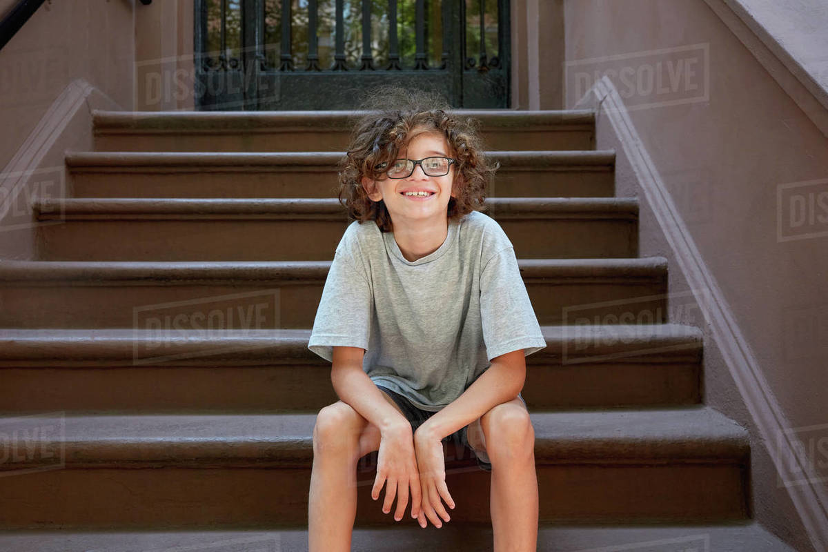 USA, New York, New York City, Boy sitting on steps in front of building ...