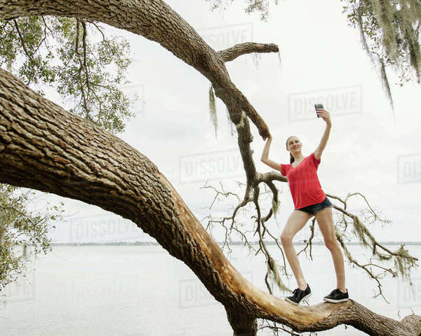 Athlete woman taking selfie on tree branch over river - Royalty-free ...