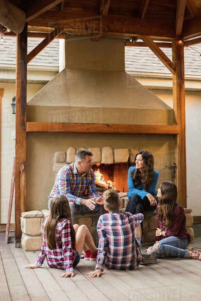 Family with children (10-11, 12-13, 16-17) sitting by fireplace ...