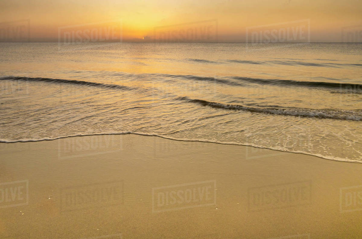 Calm ocean surf washing up onto beach at sunrise - Stock Photo - Dissolve