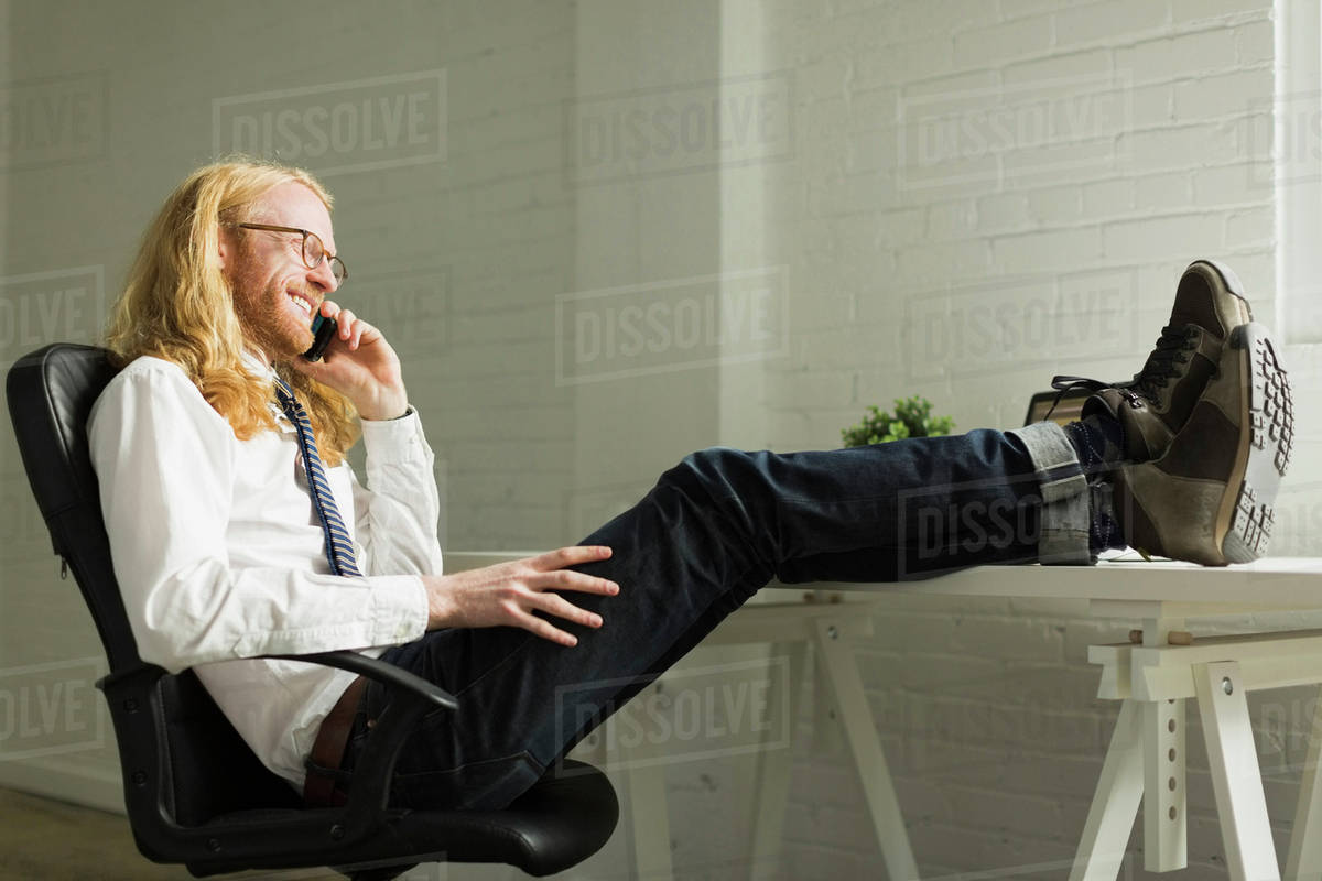 Man talking on phone with feet up on desk - Stock Photo - Dissolve