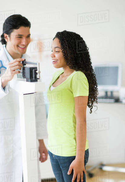 Doctor weighing female patient (10-11) - Stock Photo - Dissolve