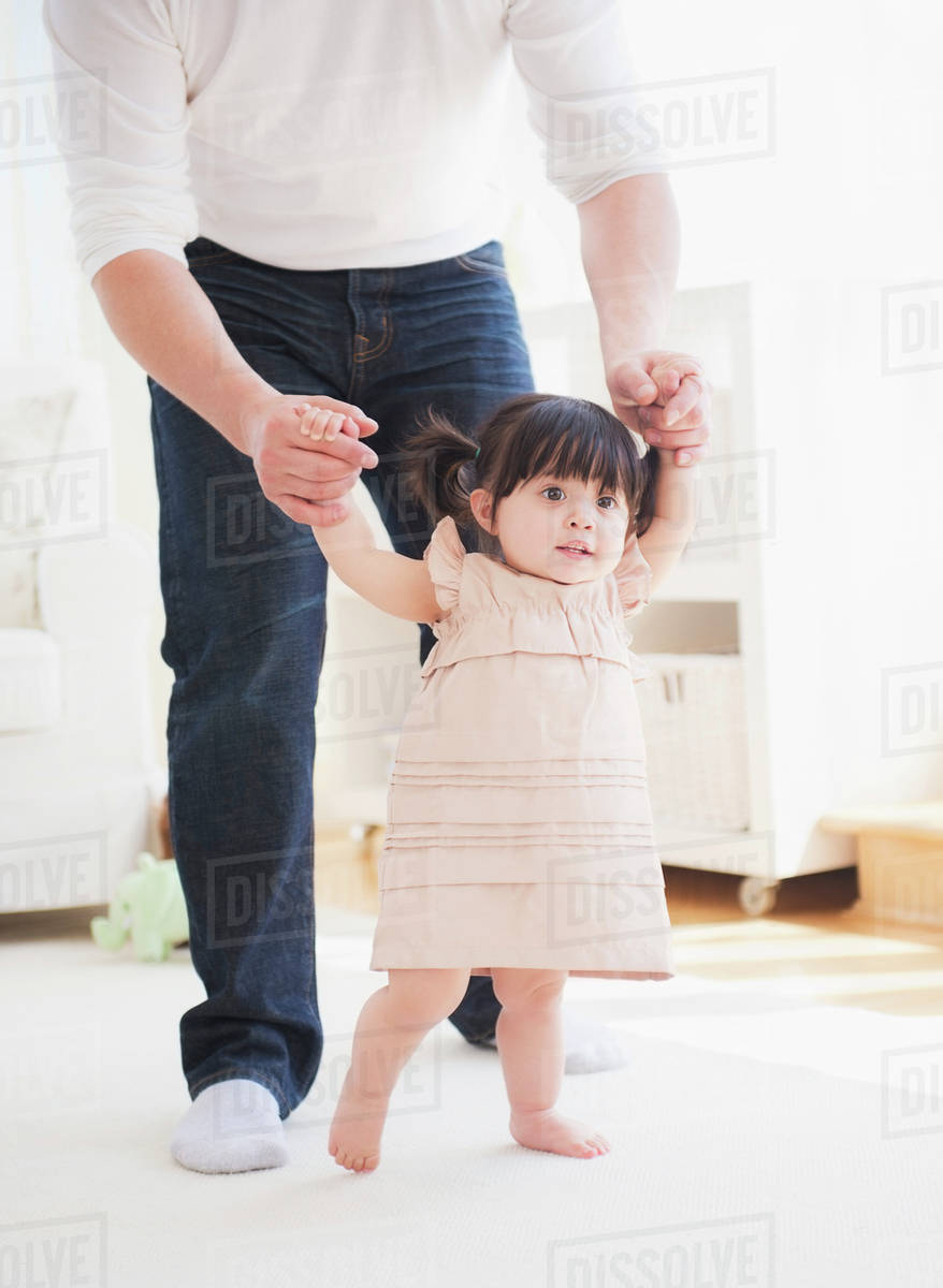 Father helping baby daughter (12-17 months) with her firsts steps ...