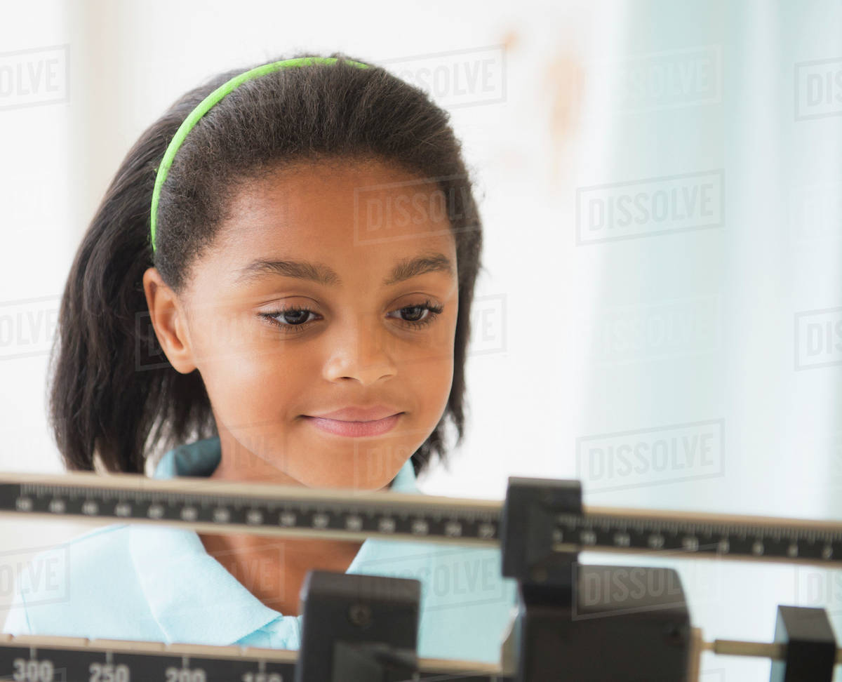 Girl (6-7 years) standing on weight scale - Stock Photo - Dissolve