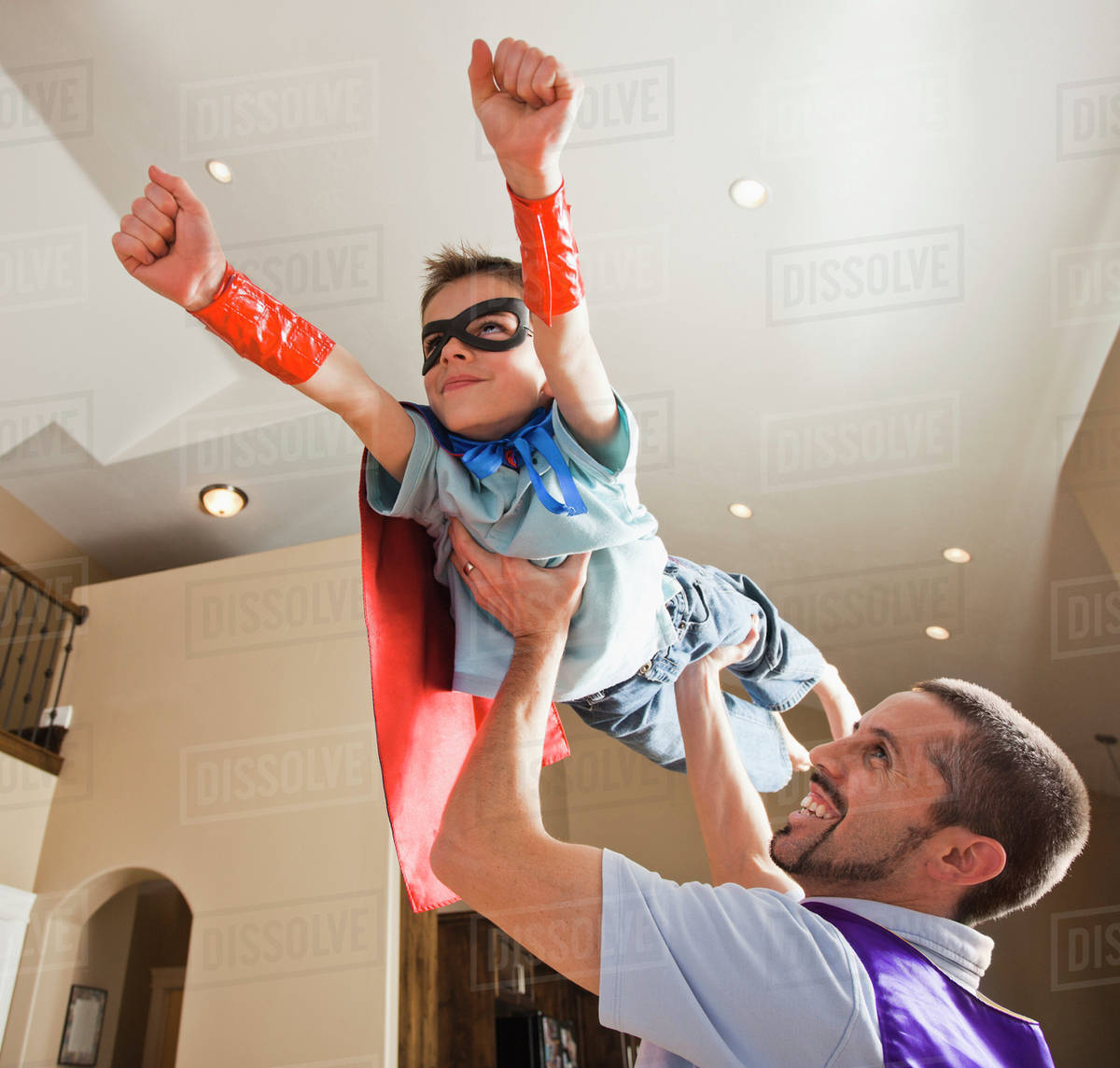 Father holding aloft his son (8-9) dressed up in fancy dress costume ...