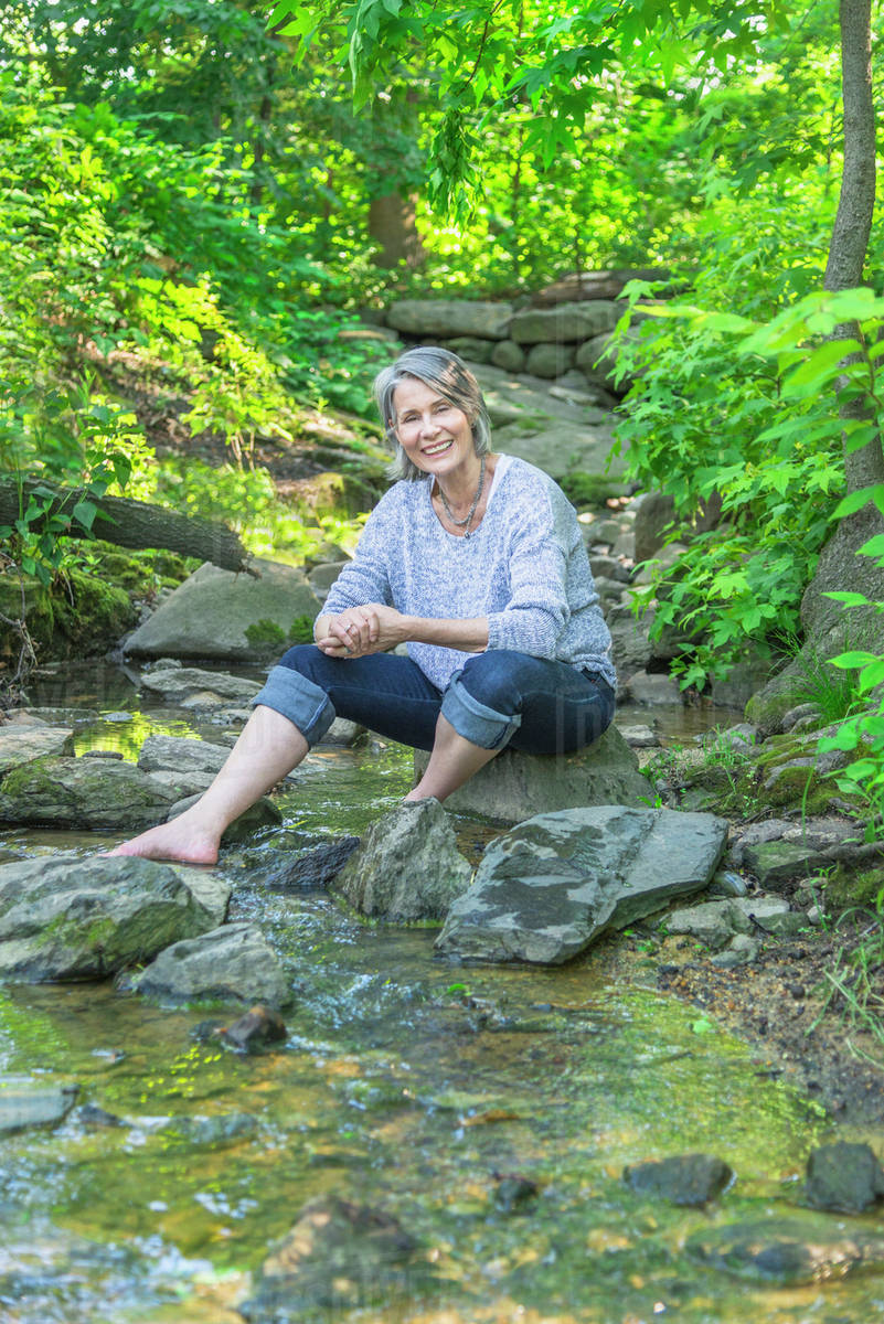 Senior woman sitting by stream - Royalty-free Stock Photo | Dissolve