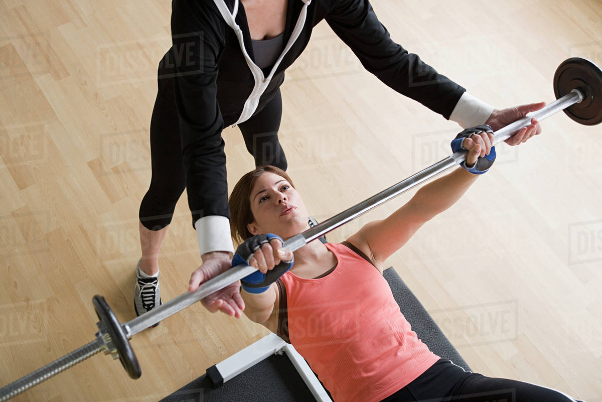 Woman lifting barbell while instructor assisting her - Royalty-free ...