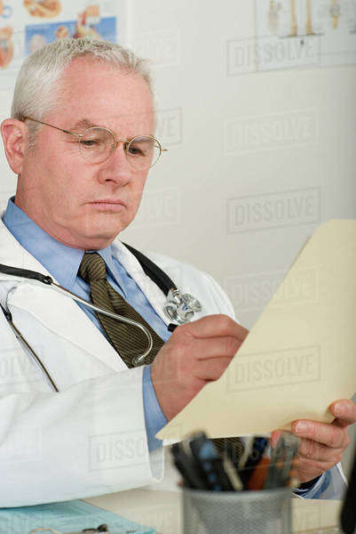 Doctor reading medical document - Stock Photo - Dissolve
