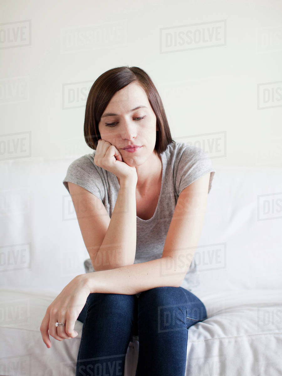 Bored young woman sitting on bed - Stock Photo - Dissolve