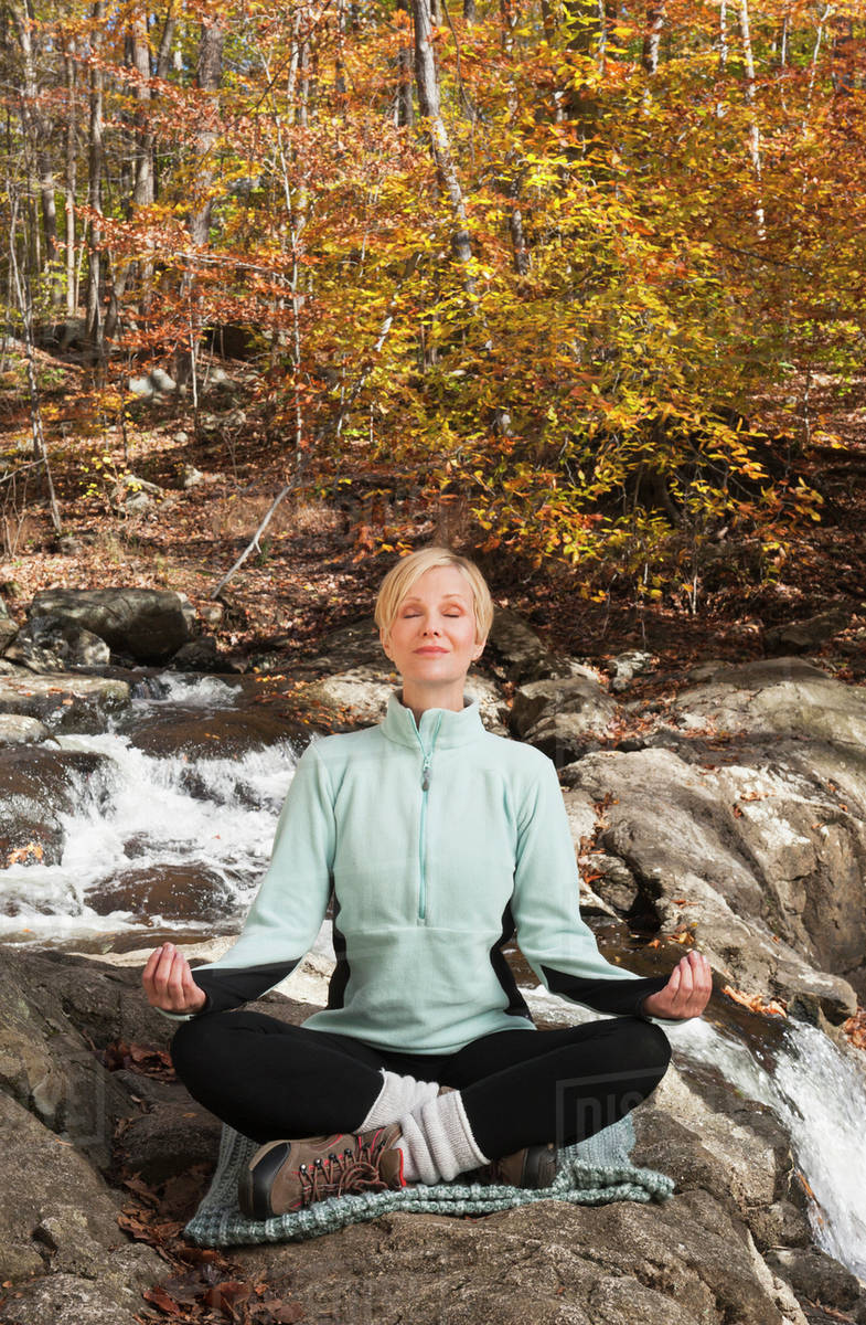 Woman meditating by stream in forest - Stock Photo - Dissolve