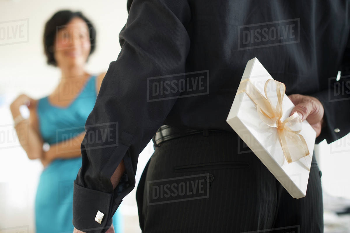 Man hiding gift box behind his back - Stock Photo - Dissolve