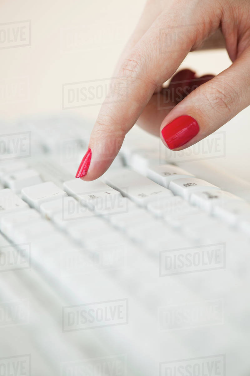 Close up of woman's finger with red nail polish typing on computer ...