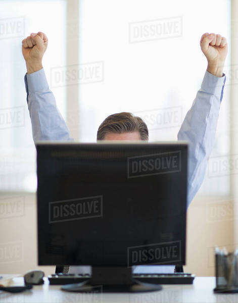 Businessman raising hands from behind computer - Stock Photo - Dissolve