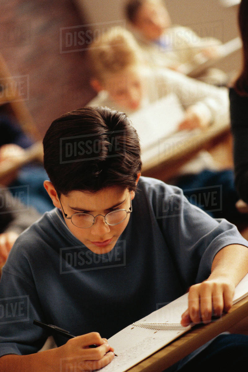 Student writing at desk in classroom - Royalty-free Stock Photo | Dissolve
